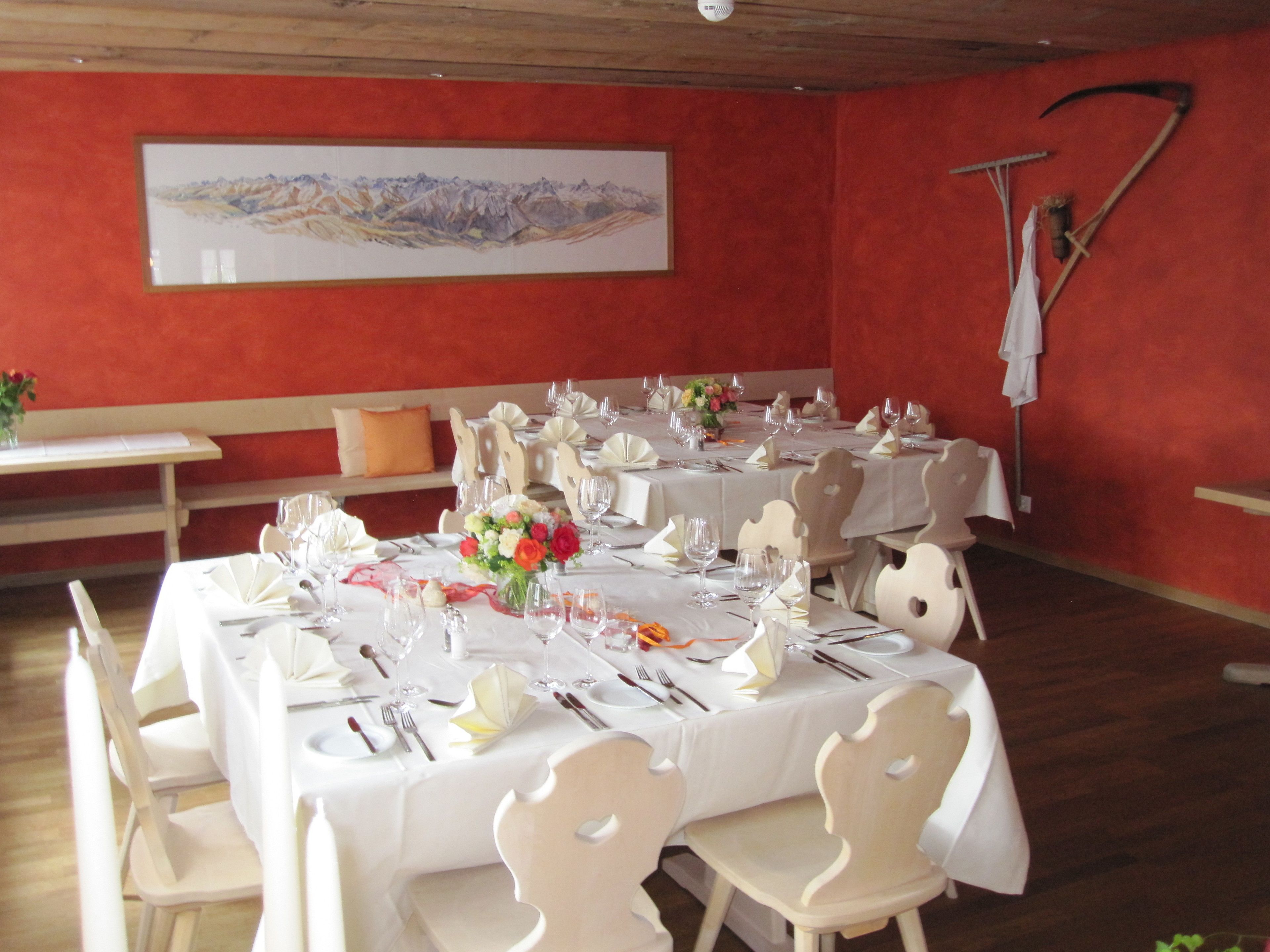 Uma sala de jantar com mesas postas para refeição, cadeiras brancas e um quadro na parede.