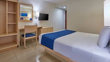 Quarto de hotel com cama, escrivaninha, cadeira, guarda-roupa, televisão e espelho.