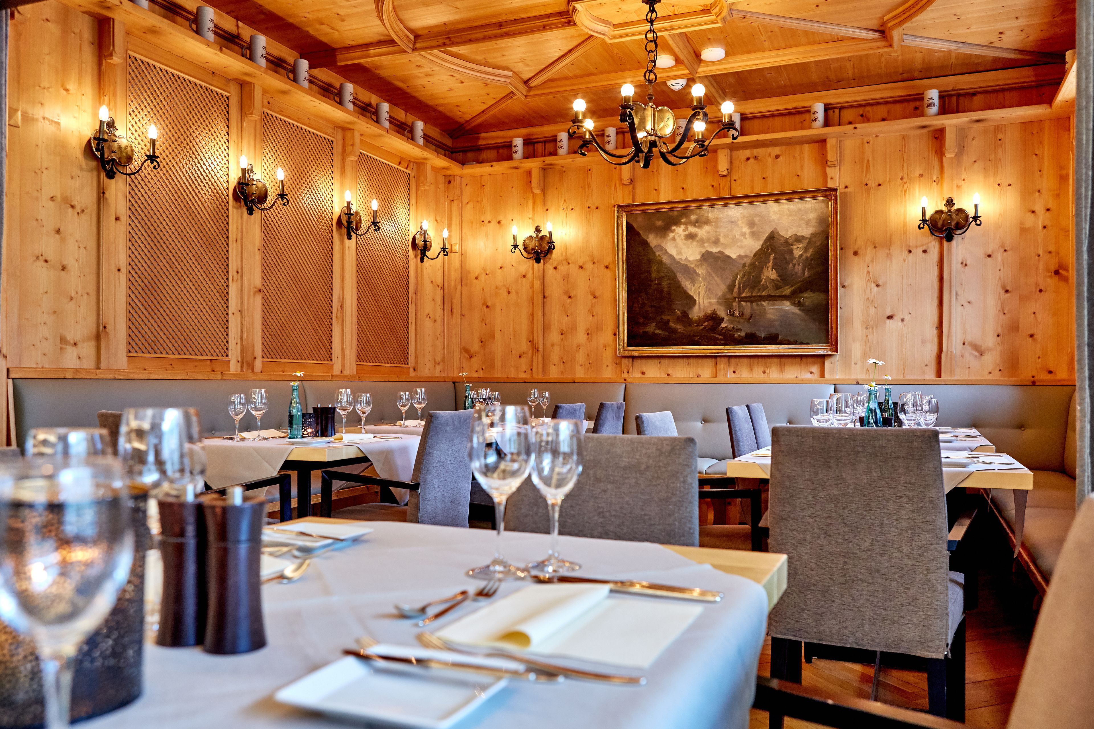 Um restaurante com painéis de madeira, lustres e uma pintura de montanha na parede.