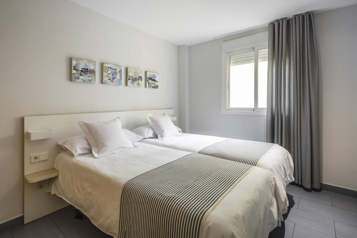 Cama de casal com roupa de cama branca e corredores listrados, uma mesa de cabeceira e uma tomada na parede.