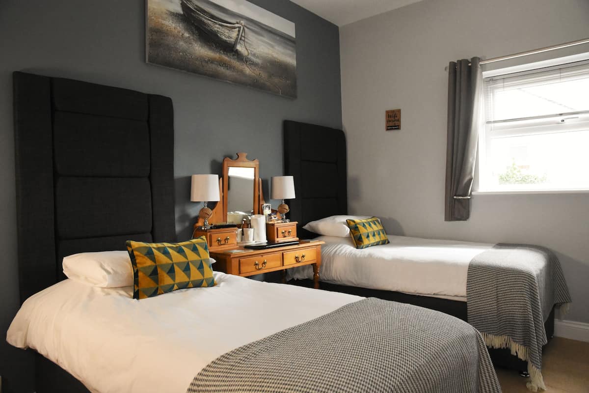Quarto de hotel com duas camas, cômoda, espelho e um quadro na parede.