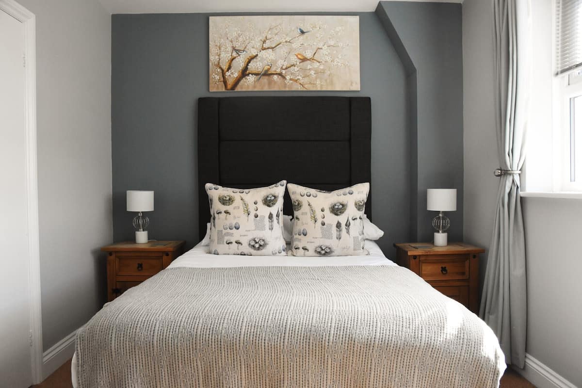 Quarto com cama, duas mesas de cabeceira, um quadro na parede e uma janela com cortinas.