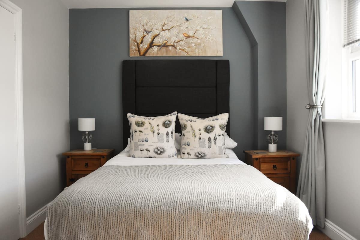 Quarto com cama grande, duas mesas de cabeceira, um quadro na parede e janela com cortinas.