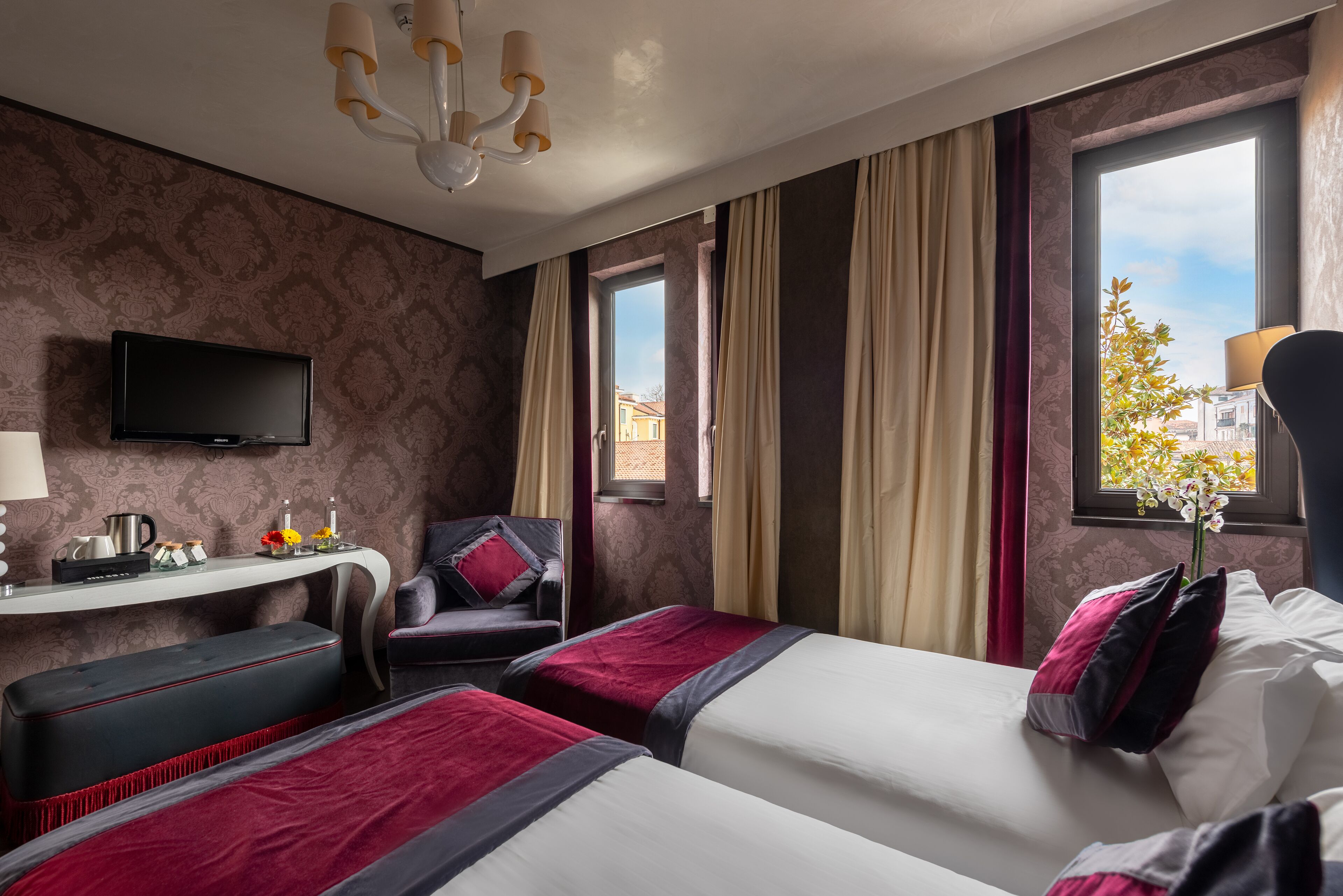 Quarto de hotel com duas camas, uma escrivaninha, uma cadeira, uma televisão e uma janela com cortinas.