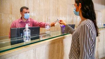 Uma receção com divisória de vidro, um frasco de álcool em gel e uma máscara facial no balcão.