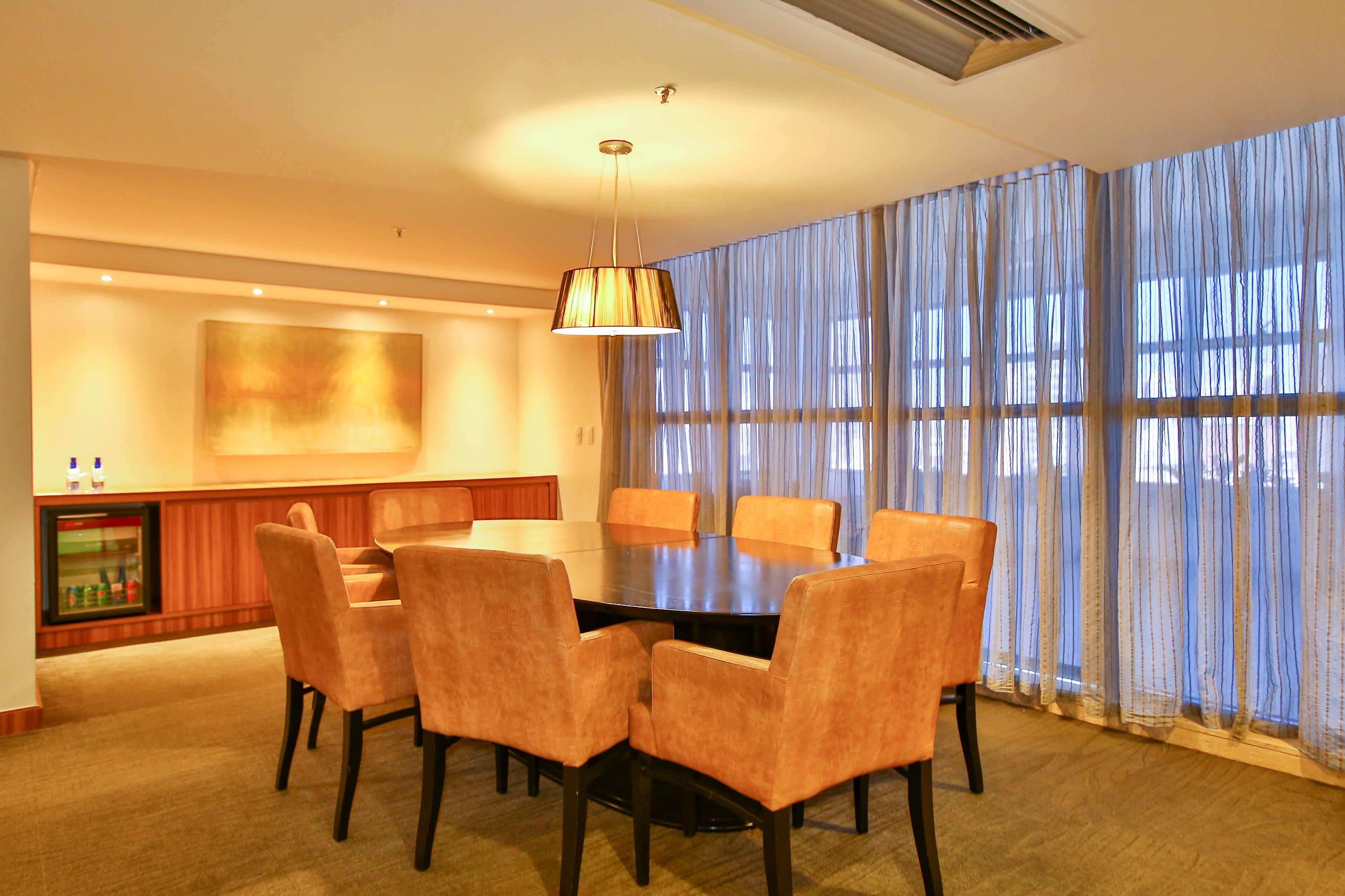 Uma sala de conferências com uma mesa grande, seis cadeiras, uma televisão e um minibar.