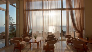 Quarto espaçoso com grandes janelas, área de jantar com cadeiras e mesa, e vista para o mar.