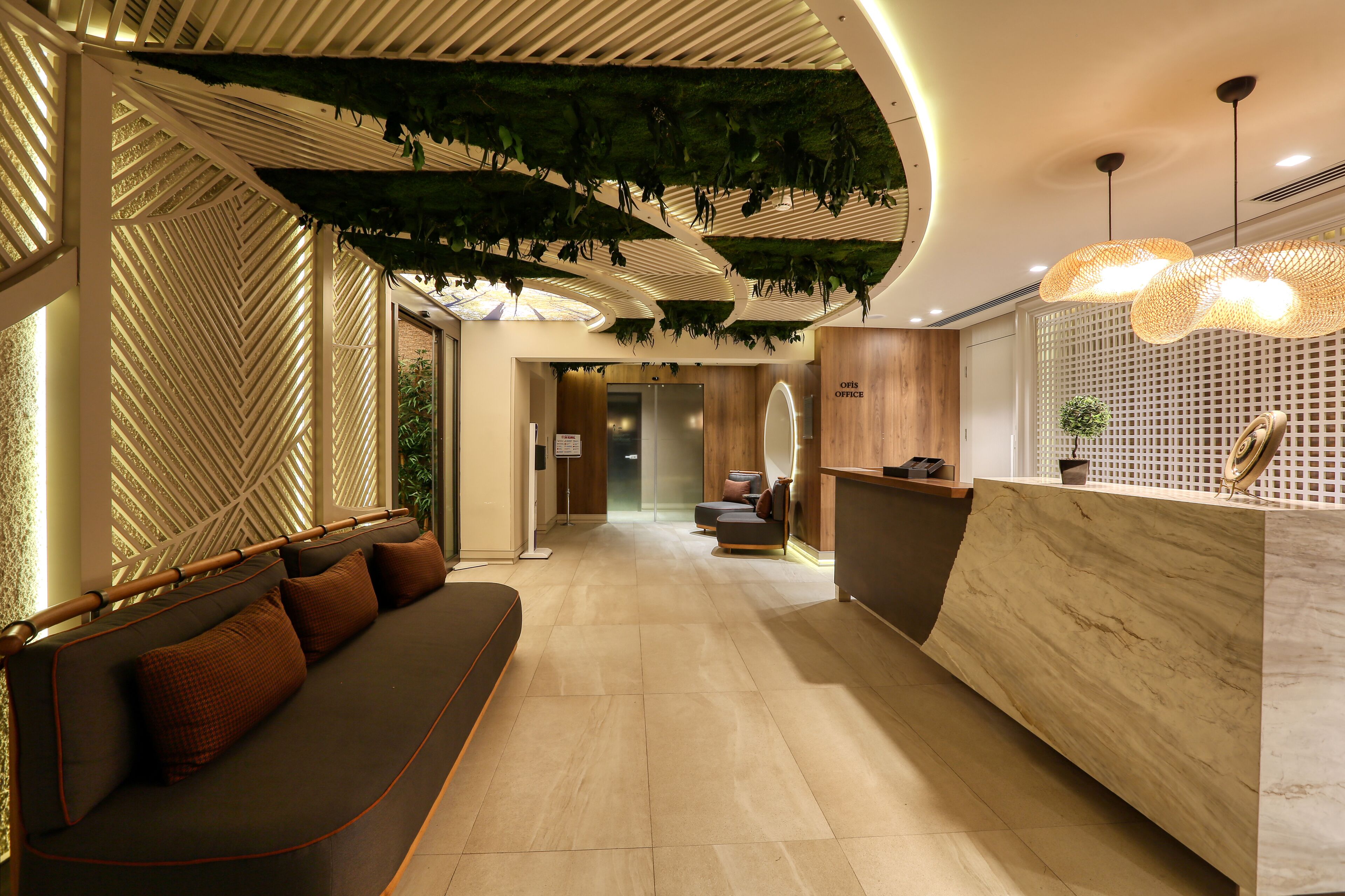 Uma área de recepção moderna, com balcão, espaço de espera com sofá e teto decorativo com plantas pendentes.