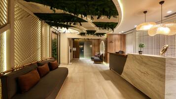 Uma área de recepção moderna, com balcão, espaço de espera com sofá e teto decorativo com plantas pendentes.