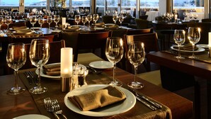 Restaurante com mesas preparadas para refeições, amplas janelas com vista e design de teto moderno.