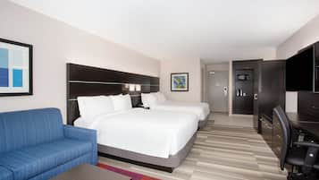 Quarto de hotel com cama, escrivaninha, poltrona, sofá e televisão.
