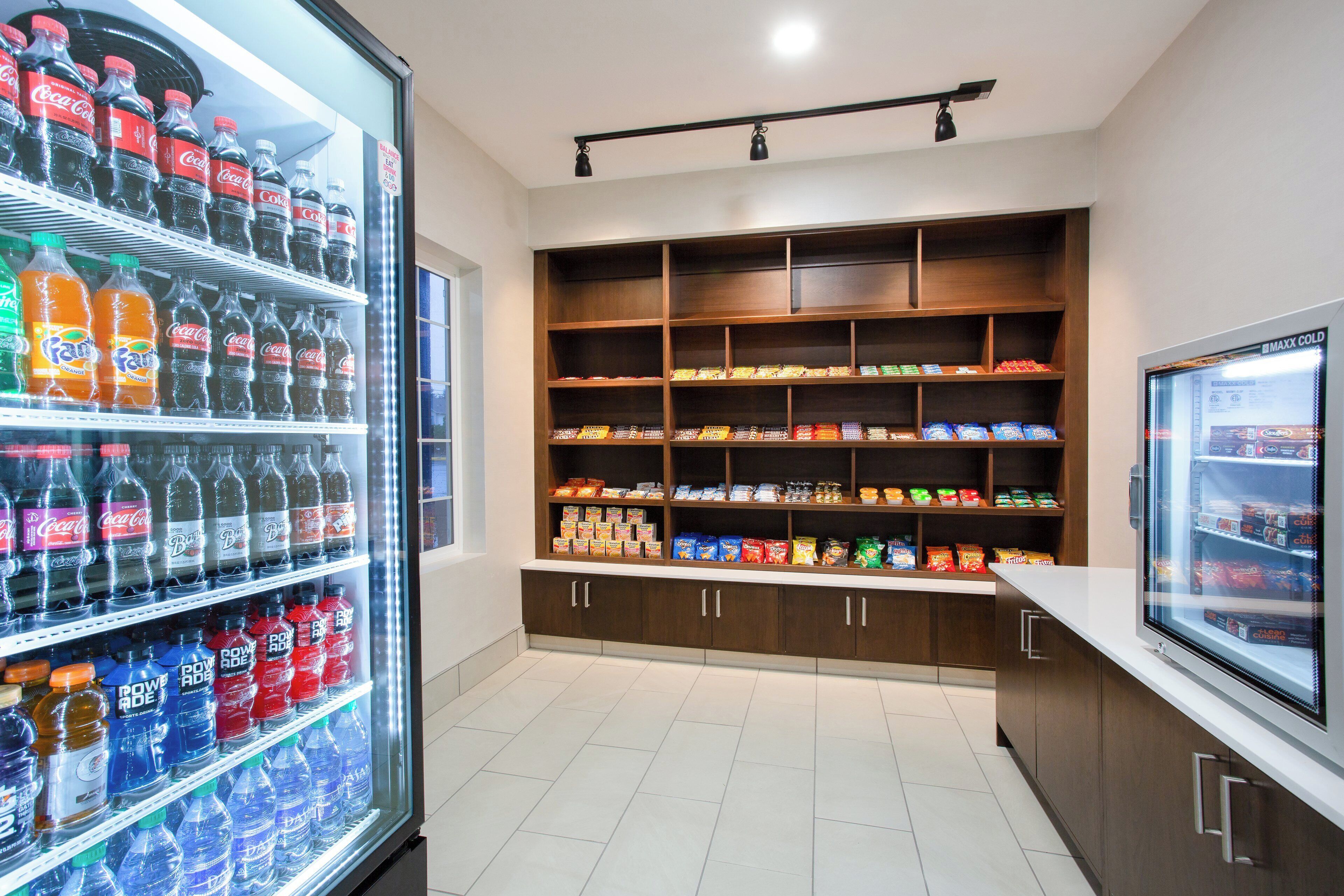Um refrigerador de bebidas cheio de diversas opções, um expositor de lanches e uma tela de menu digital.