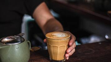 Uma pessoa segurando uma xícara com arte latte, uma chaleira verde e um balcão.