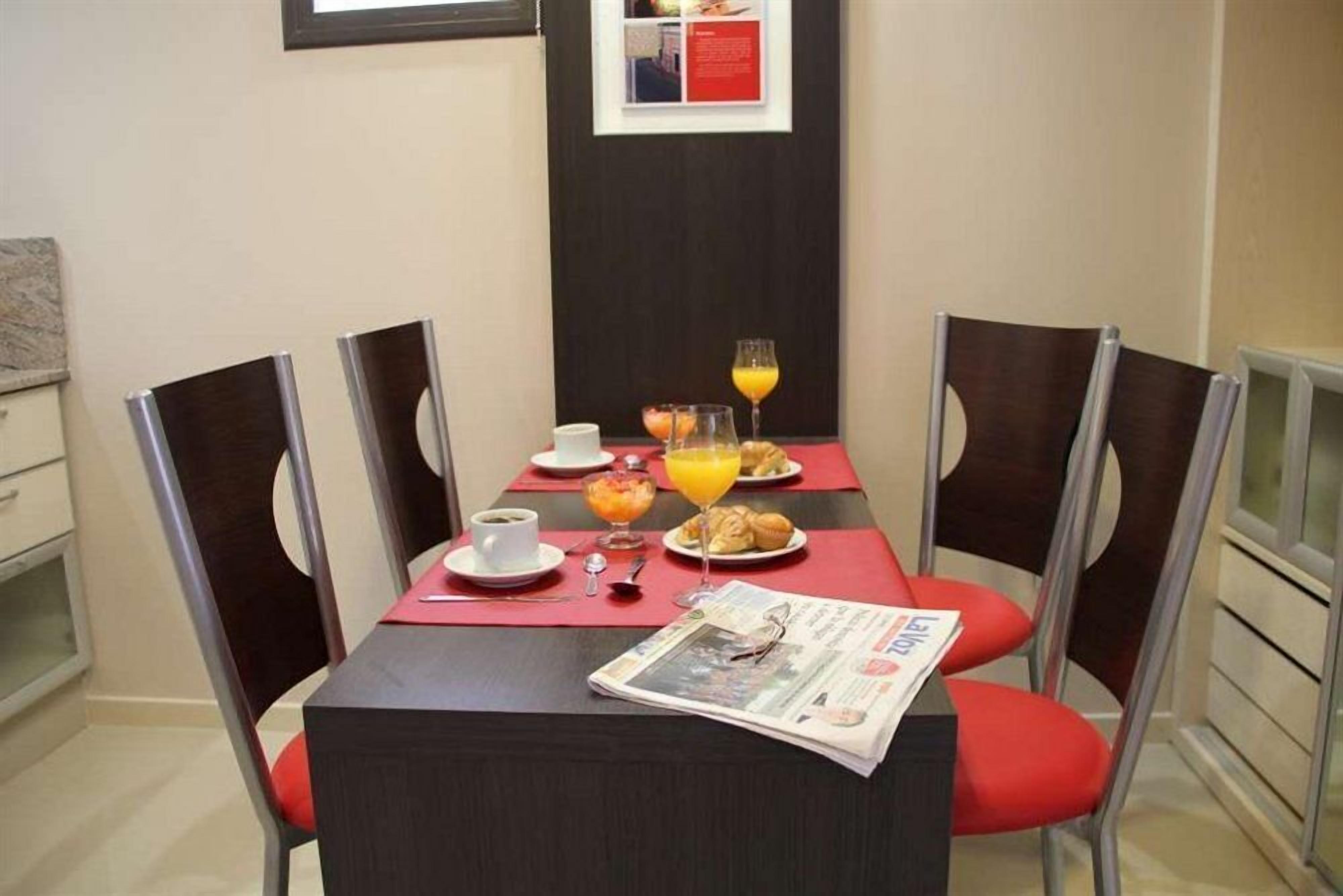 Mesa de café da manhã posta com croissants, suco de laranja e um jornal.