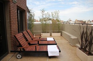 Terraço no telhado com duas poltronas de madeira, parede de tijolos e plantas em vasos.