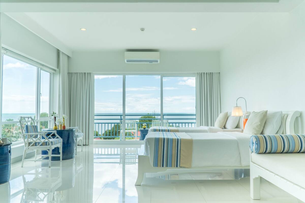 Quarto de hotel espaçoso com uma cama grande, um sofá e varanda com vista para o mar.