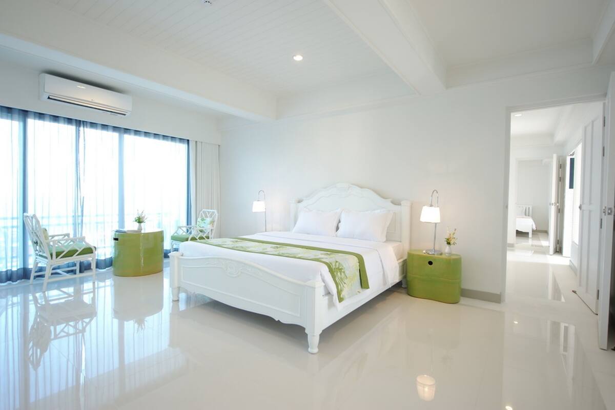 Um quarto espaçoso com uma cama grande, um espaço de estar com uma cadeira e uma mesinha, e vista para o quarto através de uma porta.