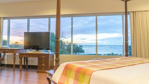 Quarto com uma cama grande, uma TV sobre uma escrivaninha de madeira e vista para o oceano.