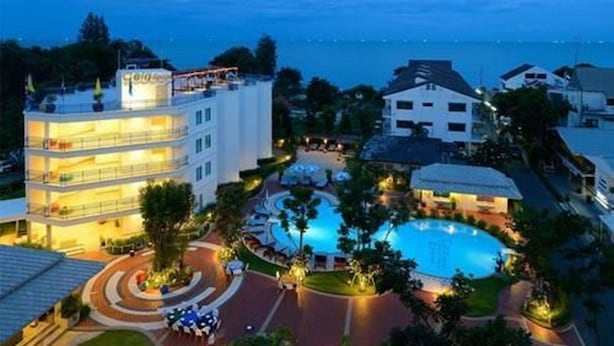 Um hotel com vários andares, piscina central rodeada por áreas ajardinadas e vista para o mar.