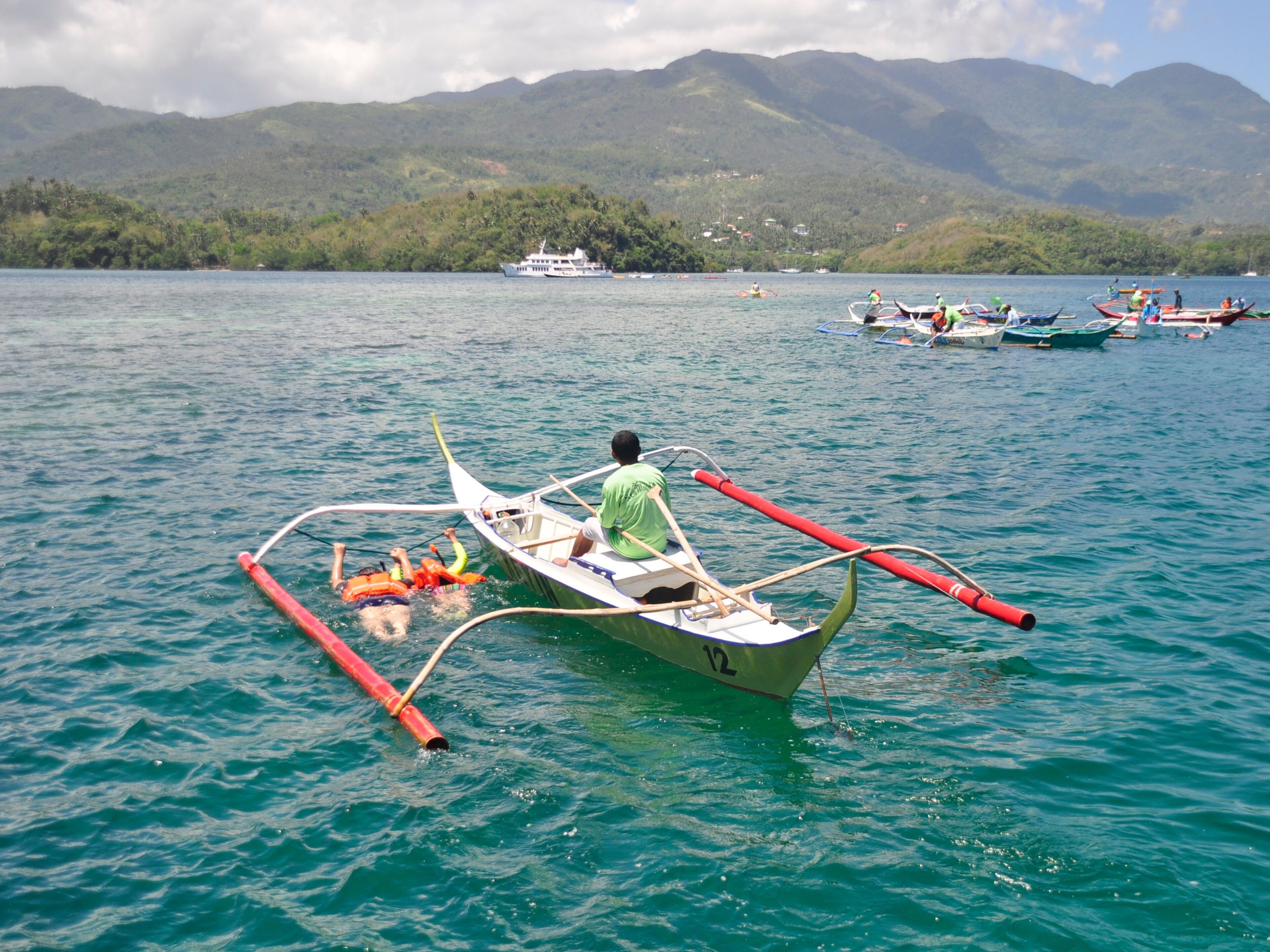 Um barco tradicional com uma pessoa remando, cercado por águas calmas e montanhas ao longe.