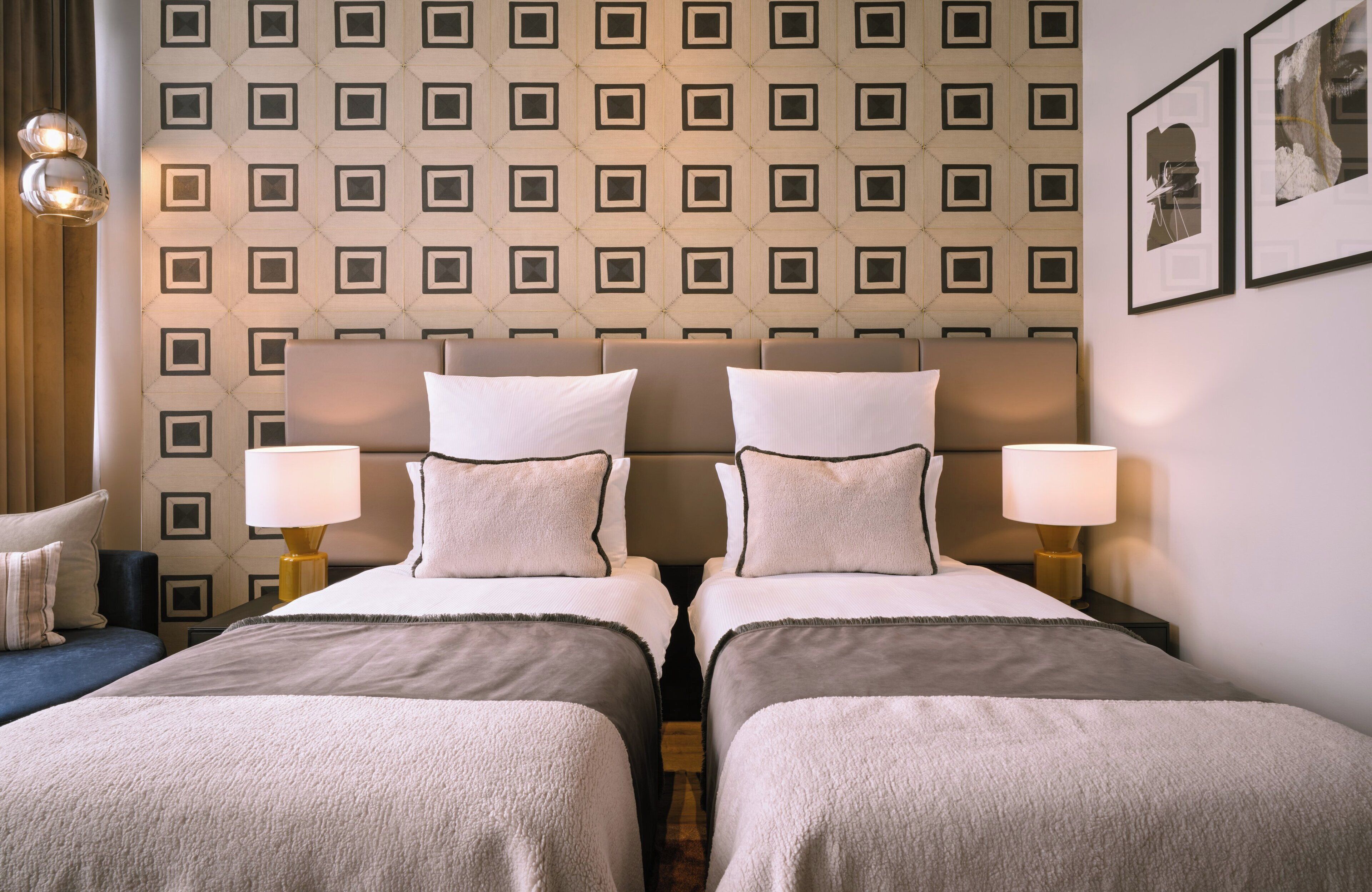 Quarto de hotel com duas camas, papel de parede estampado e duas luminárias de cabeceira.