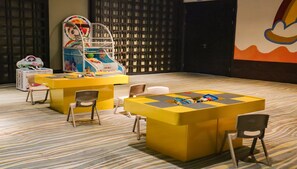 Uma área de recreação com uma mesa de brincar amarela, cadeiras e um carrossel.