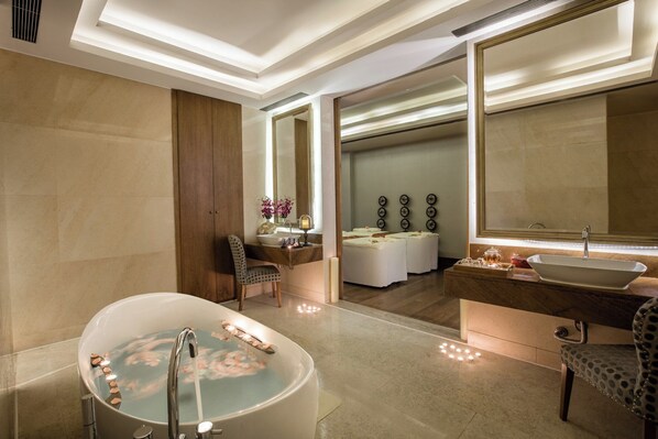 Casa de banho moderna com uma banheira independente, toucador com um espelho grande e zona de estar separada com mesa de massagem.