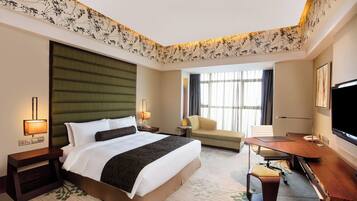 Quarto de hotel com uma cama grande, uma escrivaninha, uma cadeira, um sofá e uma televisão.