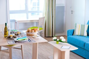 Um quarto bem iluminado com uma mesa de jantar posta para dois, um sofá azul e uma pequena mesa lateral com um vaso de flores.