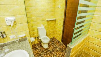 Casa de banho com azulejos amarelos, sanita branca, lavatório com bancada de granito e um secador de cabelo na parede.