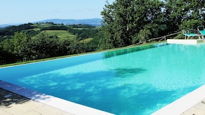 Uma piscina retangular com água azul cristalina, ladeada por um terraço de pedra.
