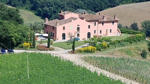 Uma villa rosa com jardim, cercada por vegetação e colinas.