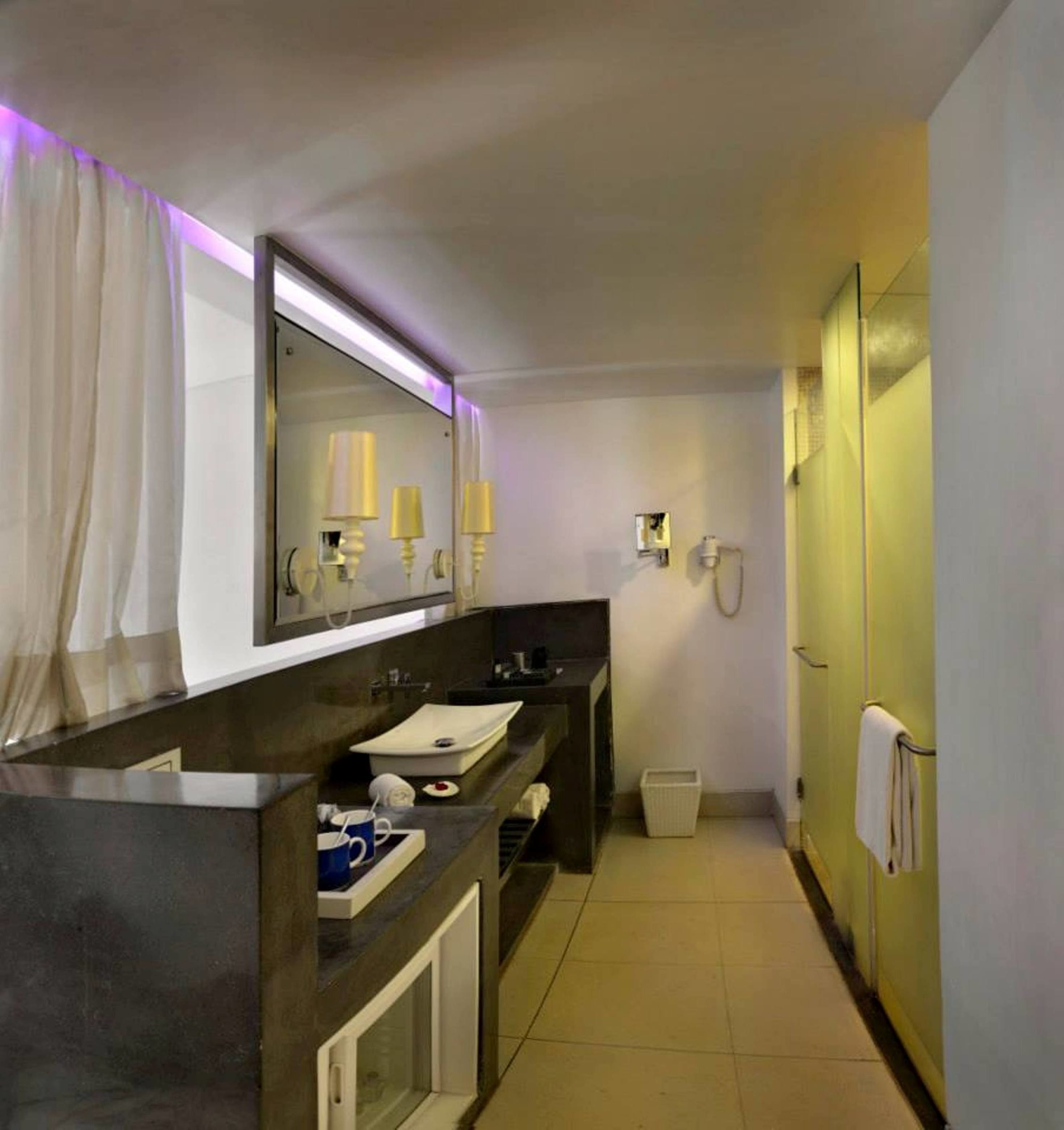 Um banheiro de hotel moderno com bancada escura, um espelho grande e uma pia branca.