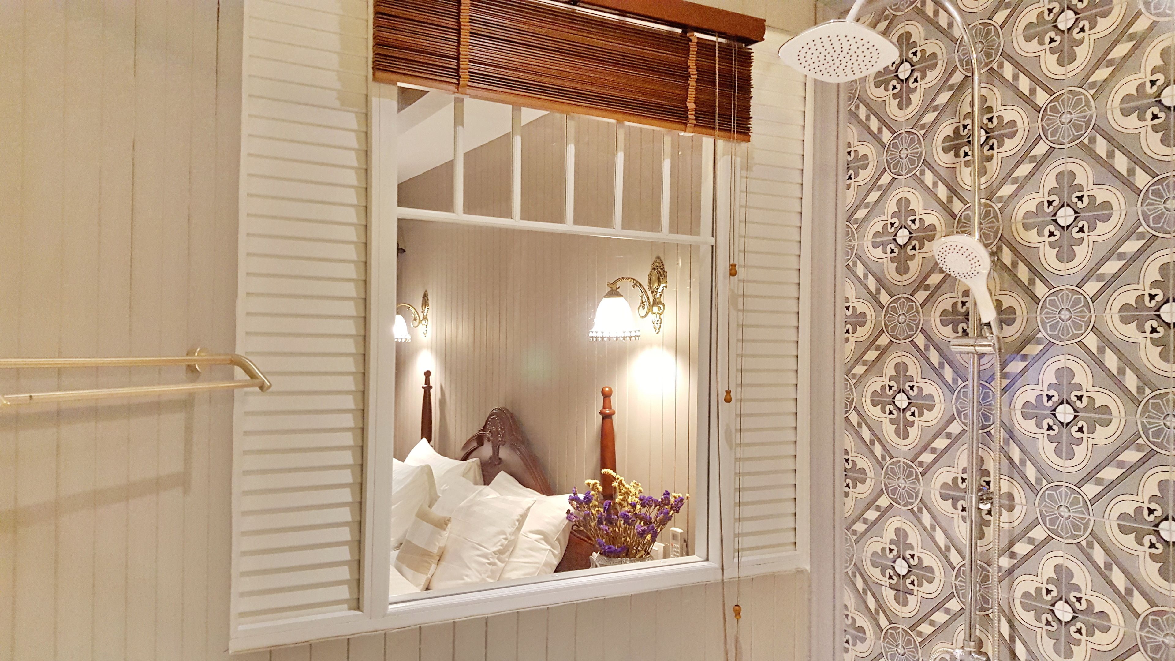 Quarto com uma janela grande, cama com roupa de cama branca, cabeceira de madeira e parede decorativa com azulejos estampados.