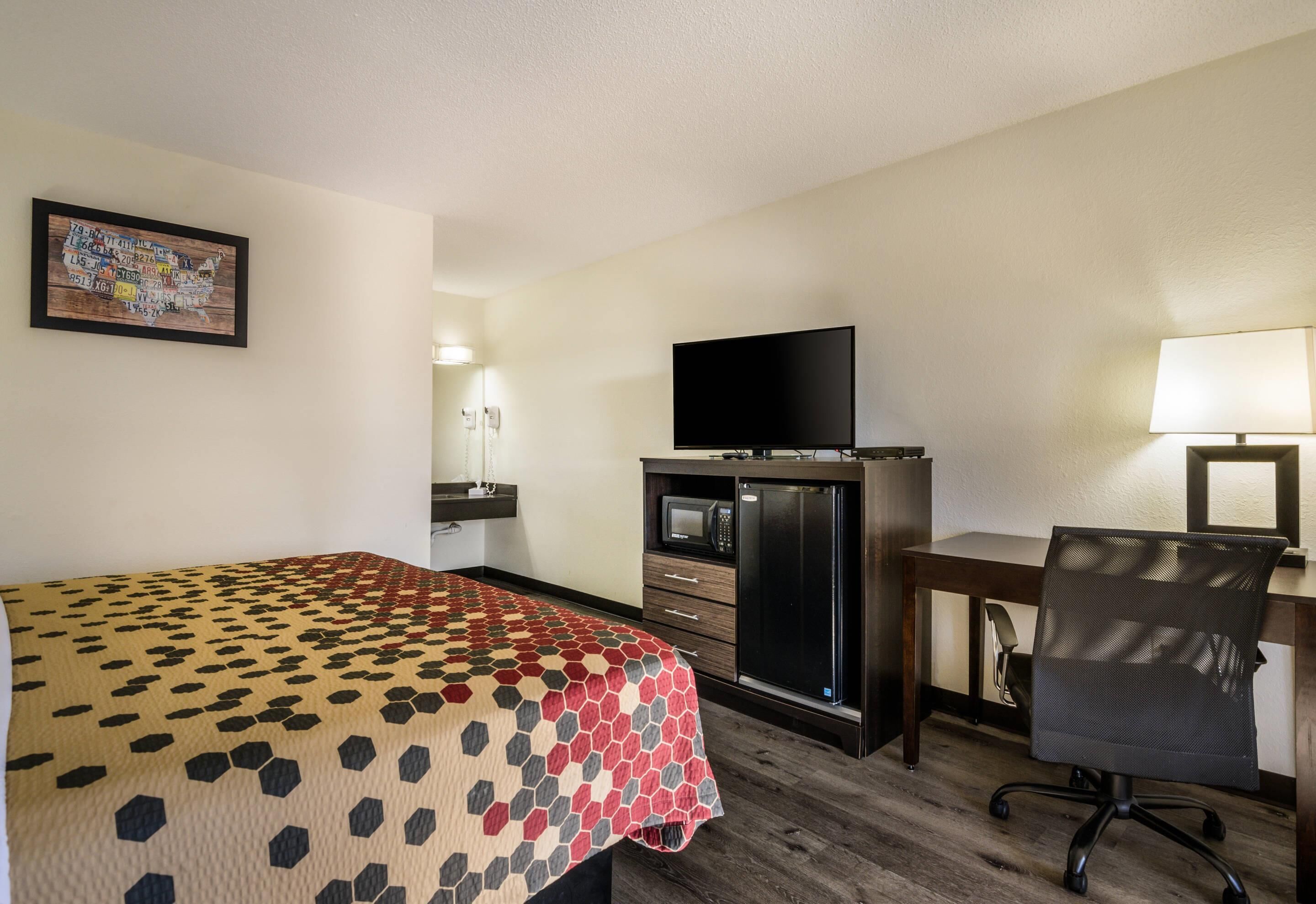 Quarto de hotel com cama, escrivaninha e cadeira, televisão, micro-ondas e frigorífico.