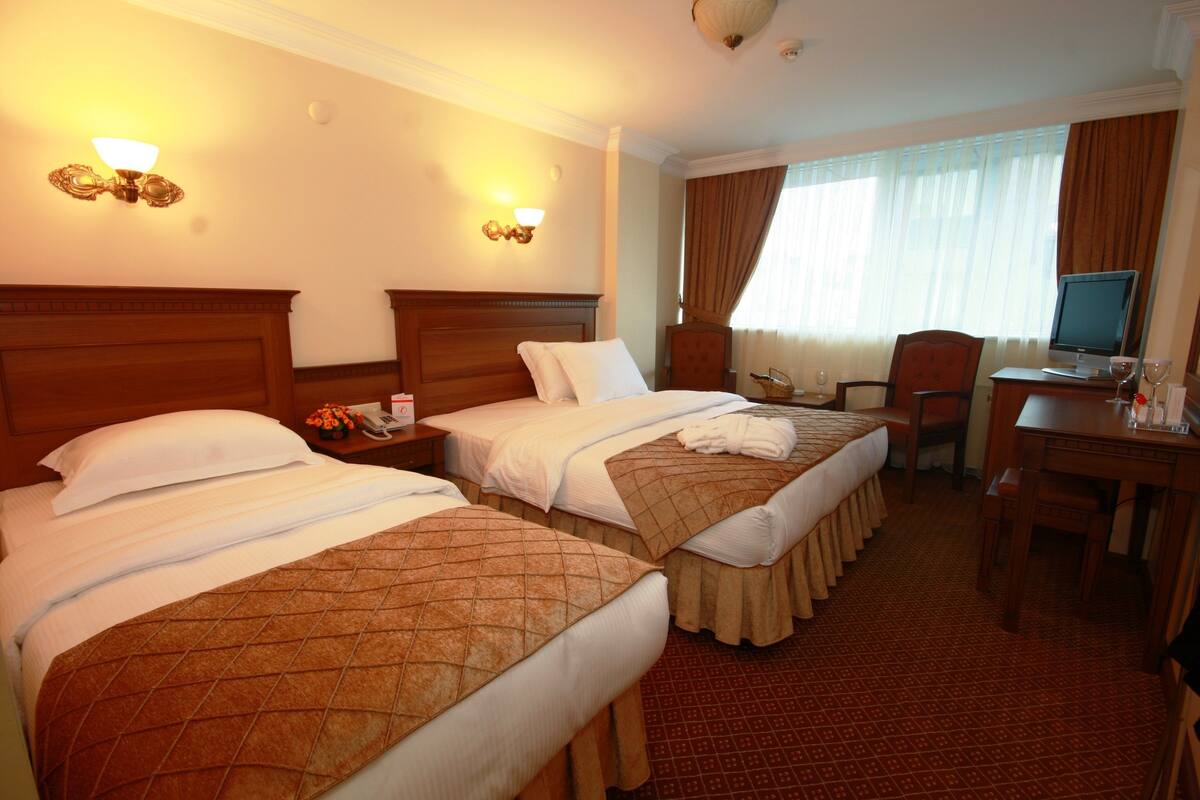 Quarto de hotel com duas camas, uma escrivaninha, uma cadeira e uma televisão.