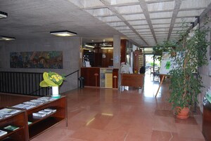 Um hall amplo com balcão de recepção, escada e um mural na parede.