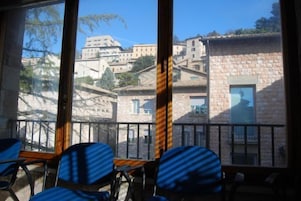 Quarto com vista para uma vila numa colina, com edifícios de pedra e varanda com cadeiras.