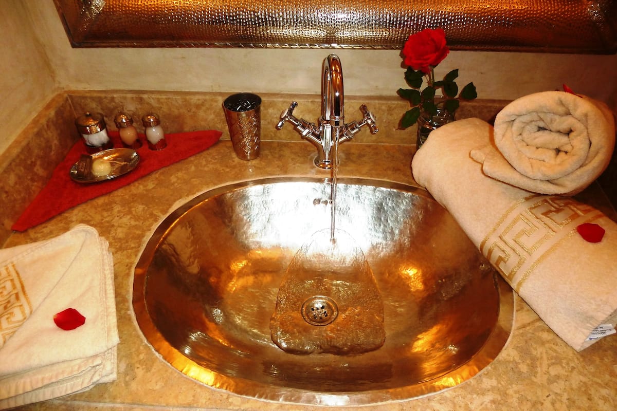 Uma pia de banheiro com uma torneira, uma rosa vermelha e uma toalha enrolada.
