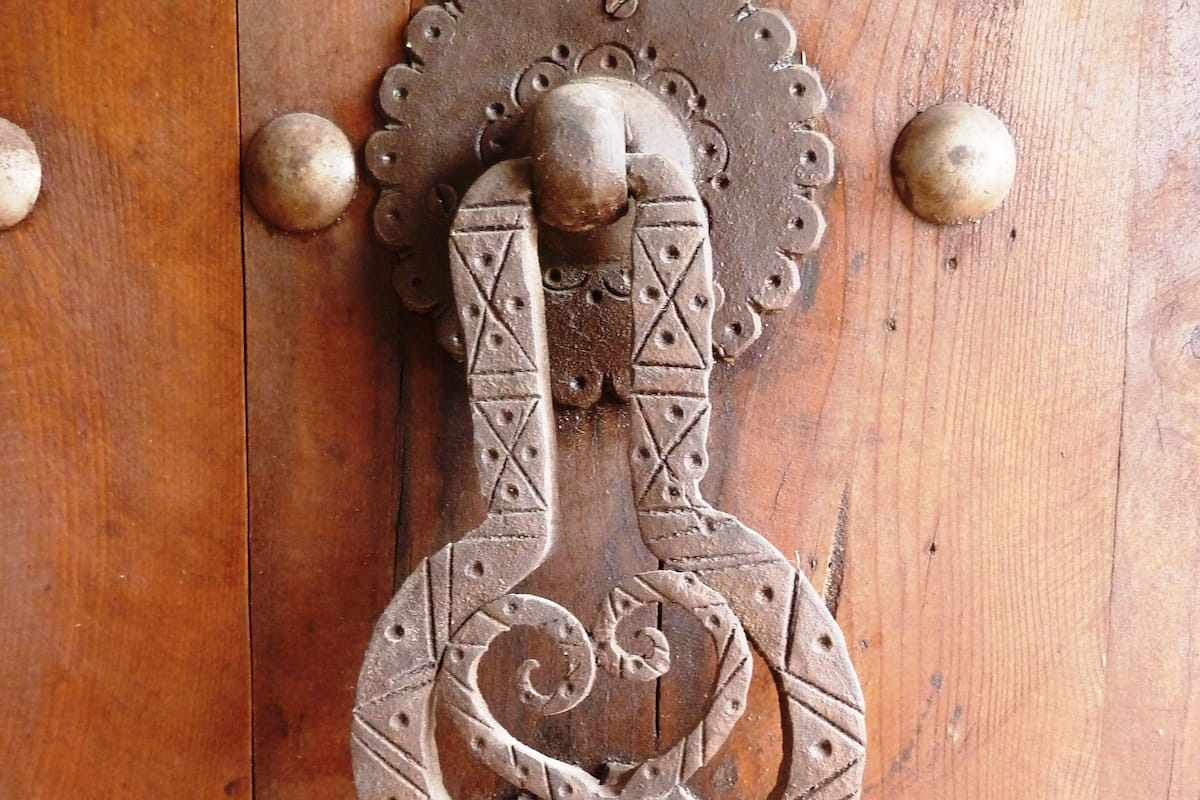 Uma porta de madeira com uma maçaneta de metal decorada com padrões geométricos e um design em espiral.