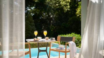 Mesa à beira da piscina com dois copos de sumo de laranja, um prato de comida e uma cadeira com uma toalha.