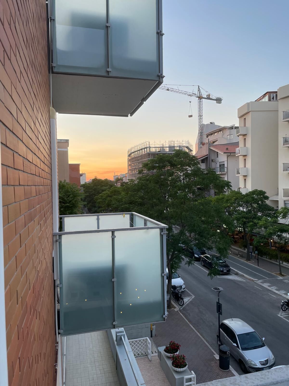 Uma varanda com vista para um canteiro de obras e uma rua com carros estacionados.