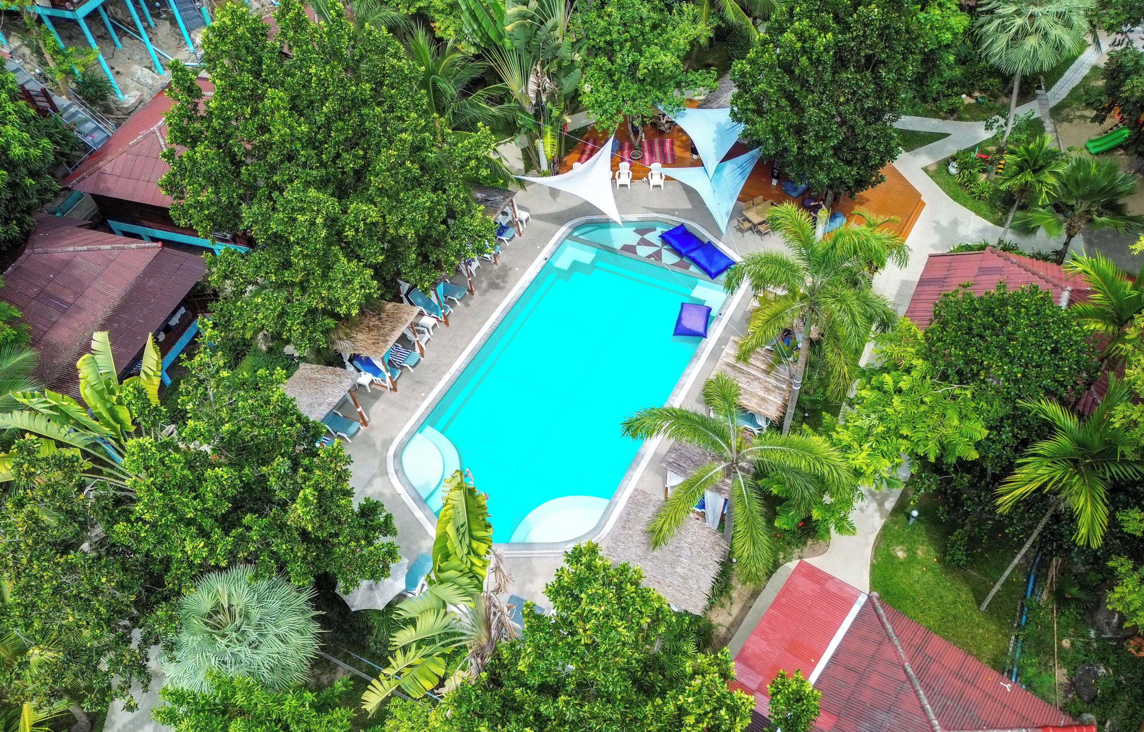 Vista aérea de um resort com piscina central cercada por vegetação exuberante e palmeiras.
