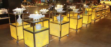 Disposição de buffet com várias estações de comida, cada uma com uma vitrine de vidro e uma tigela branca.