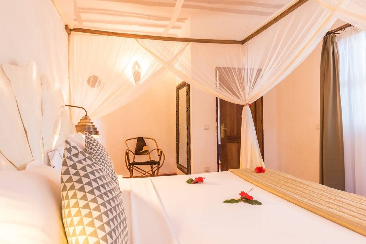 Quarto de hotel com cama, cadeira, espelho e janela com cortinas.