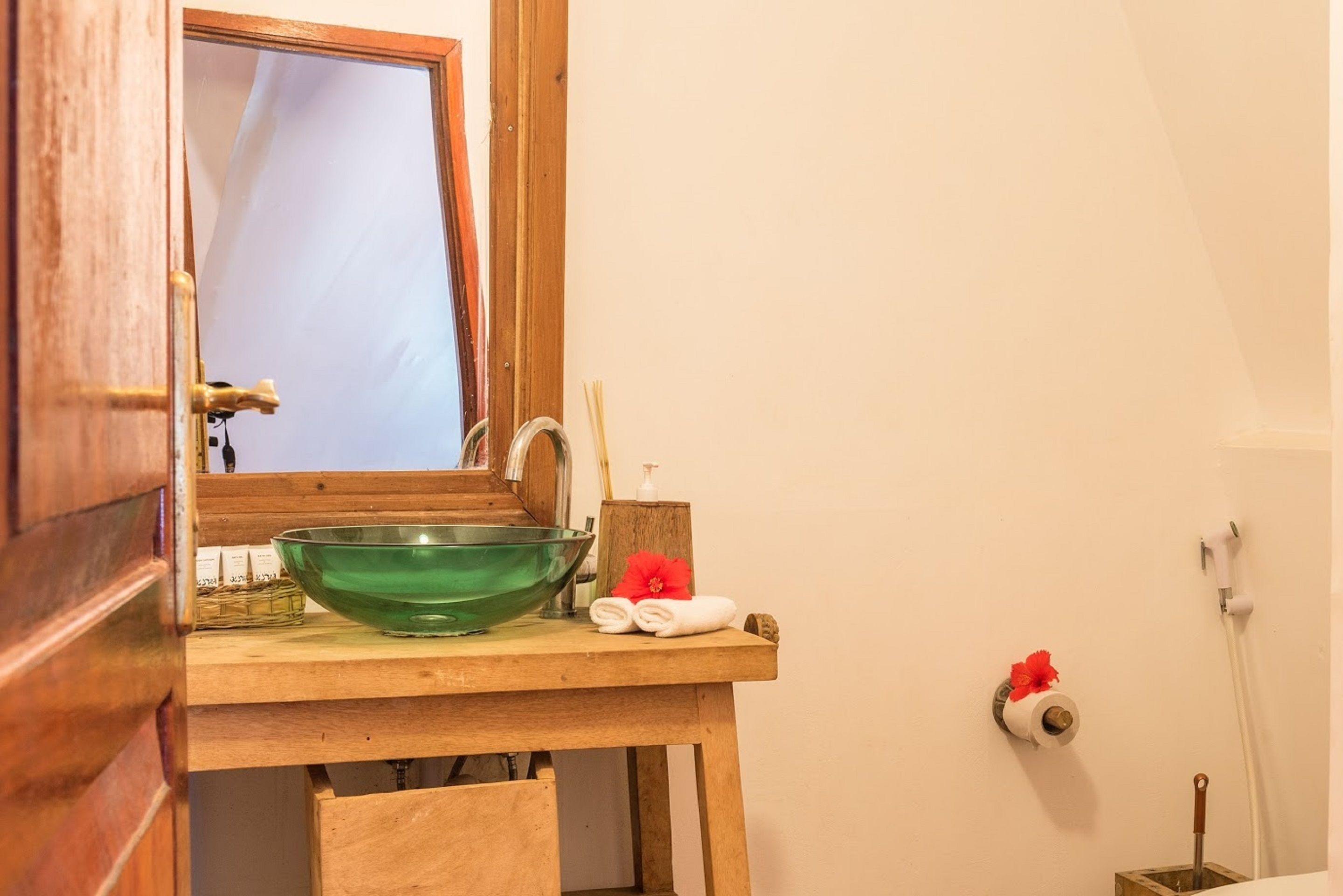 Um lavatório de casa de banho em madeira com uma bacia de vidro verde, um espelho e um porta-toalhas.