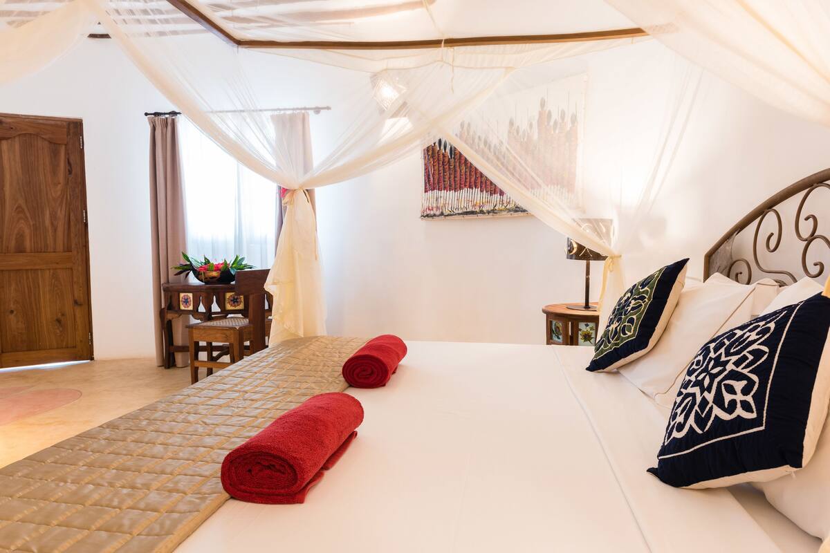 Quarto com cama, mesa de cabeceira, cadeira e porta de madeira.
