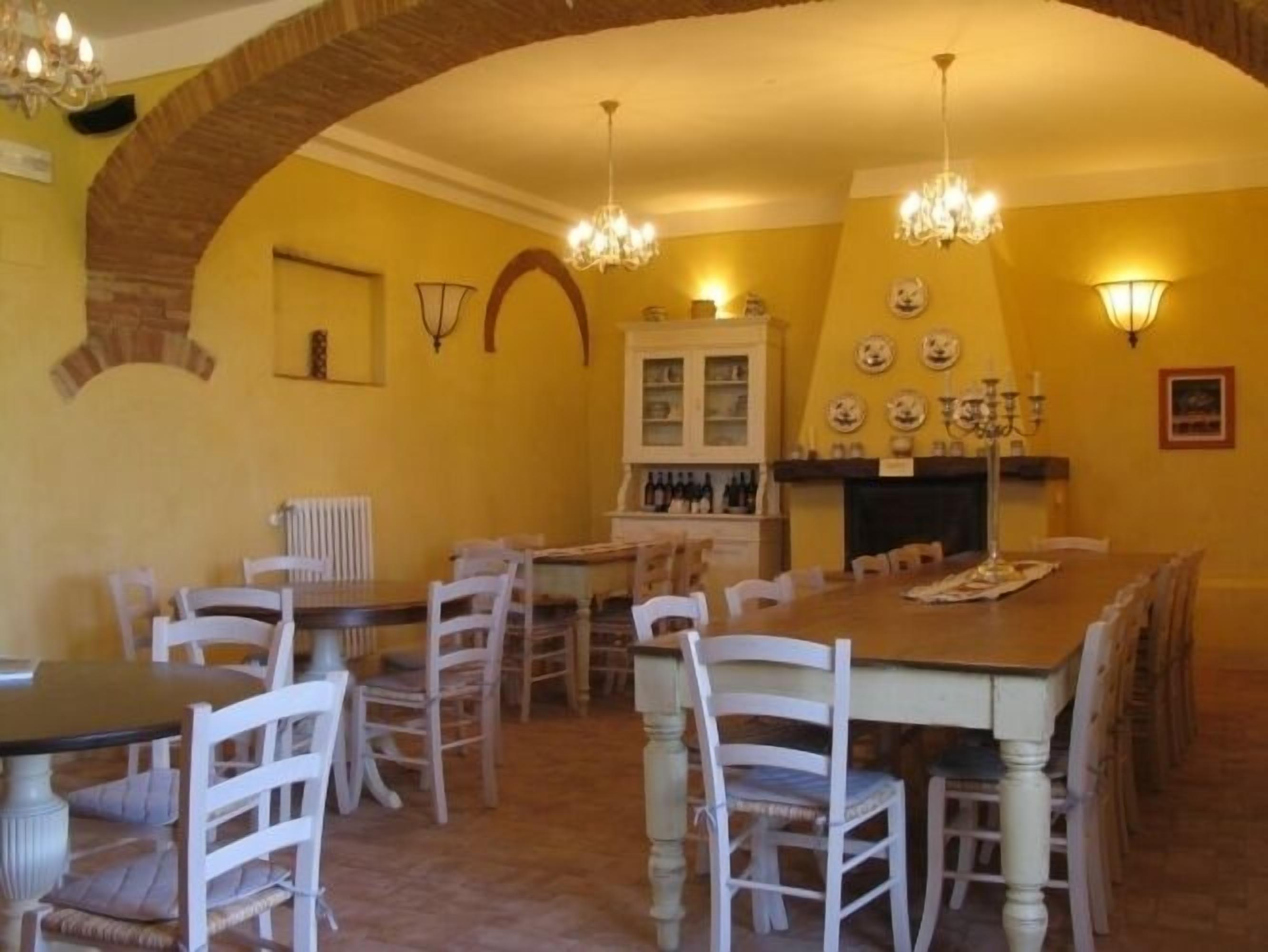 Uma sala de jantar com uma mesa grande e várias cadeiras, um armário com garrafas e luminárias fixadas na parede.