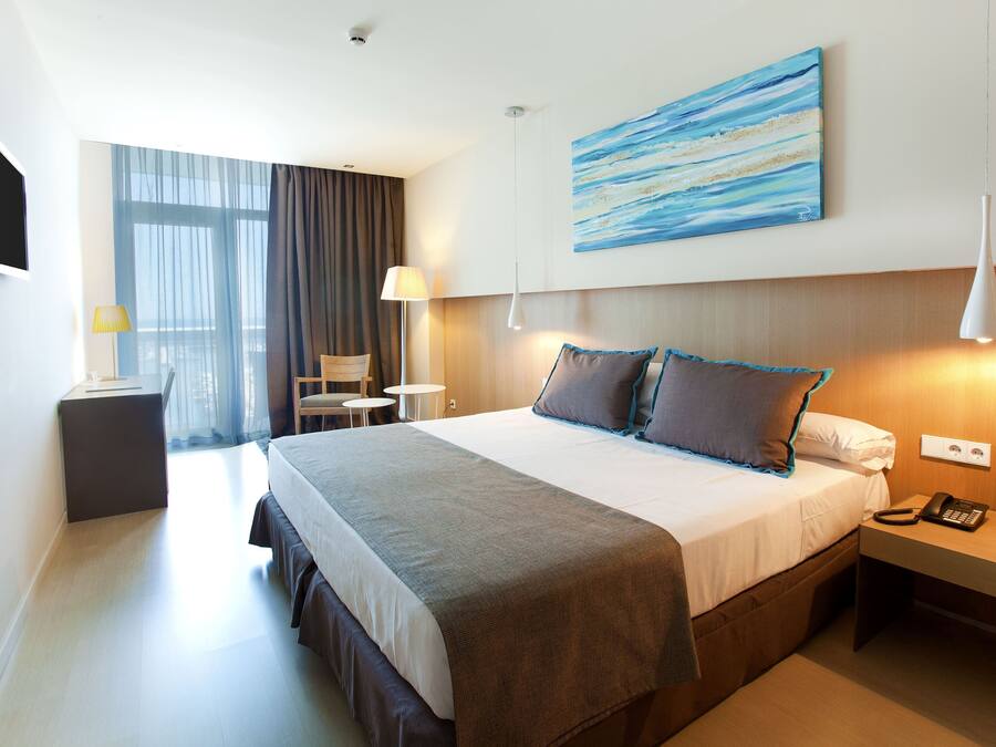 Quarto de hotel com cama, mesa de cabeceira, abajur e um quadro na parede.