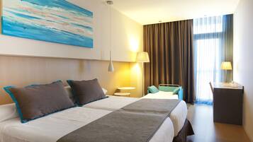 Quarto de hotel com duas camas, uma escrivaninha, uma cadeira, um abajur e um quadro na parede.